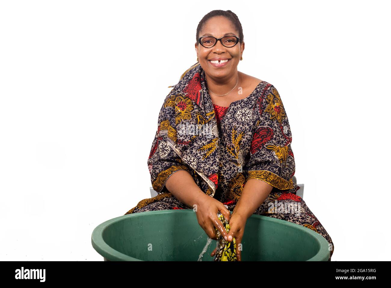 smiling african woman sitting and washing clothes in a big green bowl ...