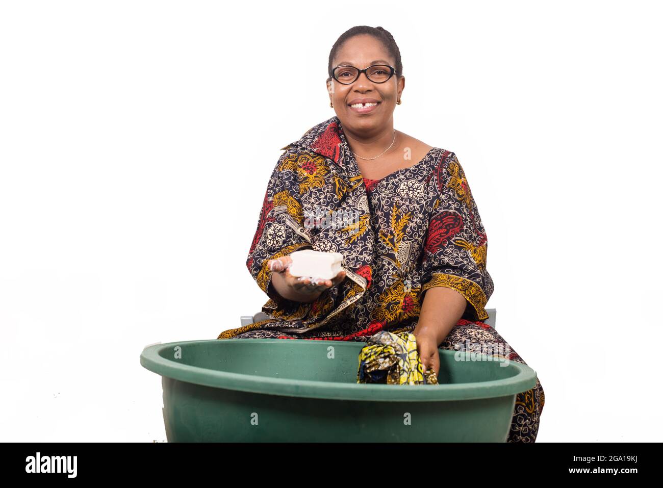 Smiling african woman sitting and washing clothes in a green bowl grade ...