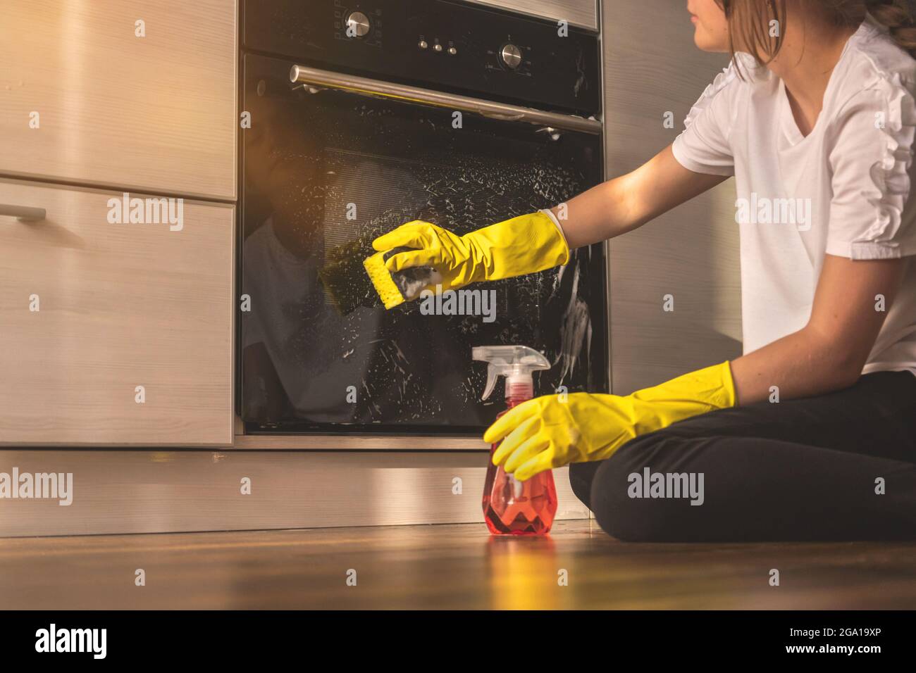 Young girl cleaning the kitchen oven with spray bottle detergent ...