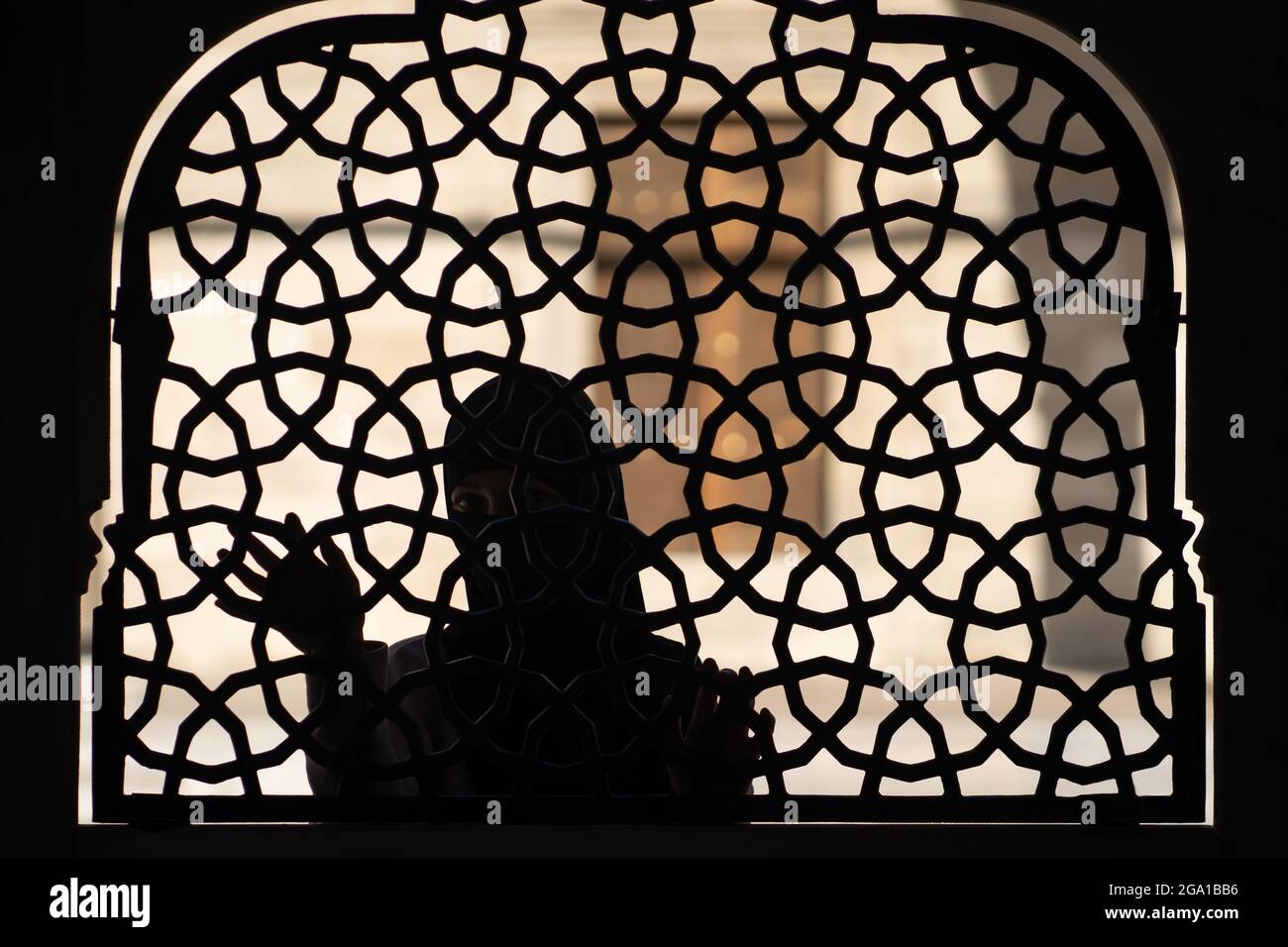 A Muslim girl in a black hijab stands behind a patterned wrought-iron ...