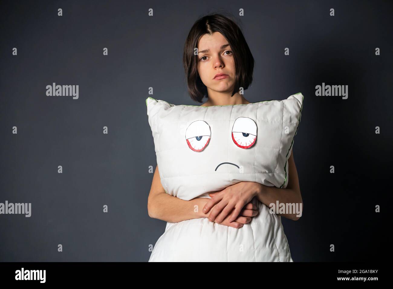 Cute sad young girl hugs a white pillow with painted eyes and face ...