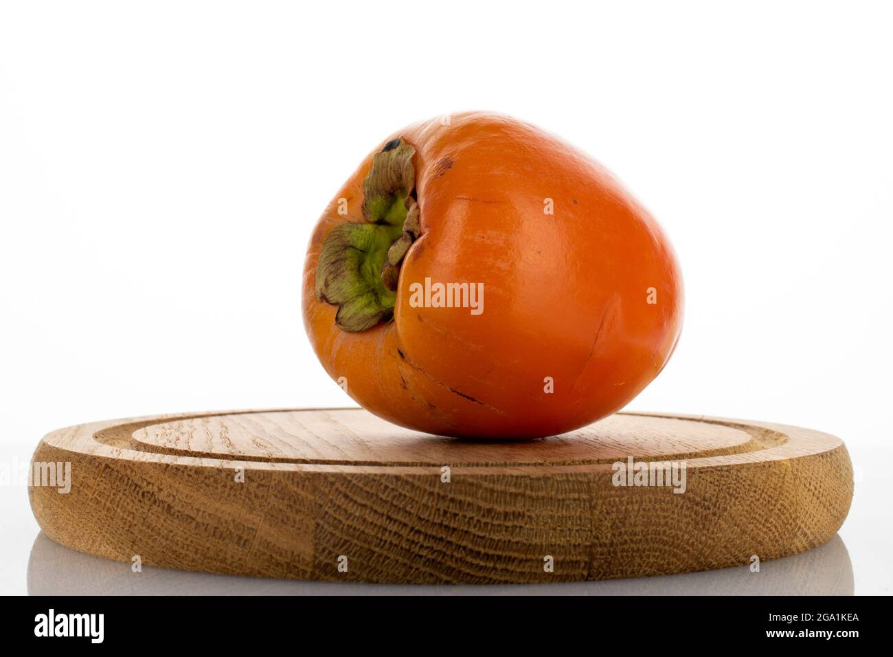 One ripe organic persimmon on a round wooden tray, close-up, isolated ...