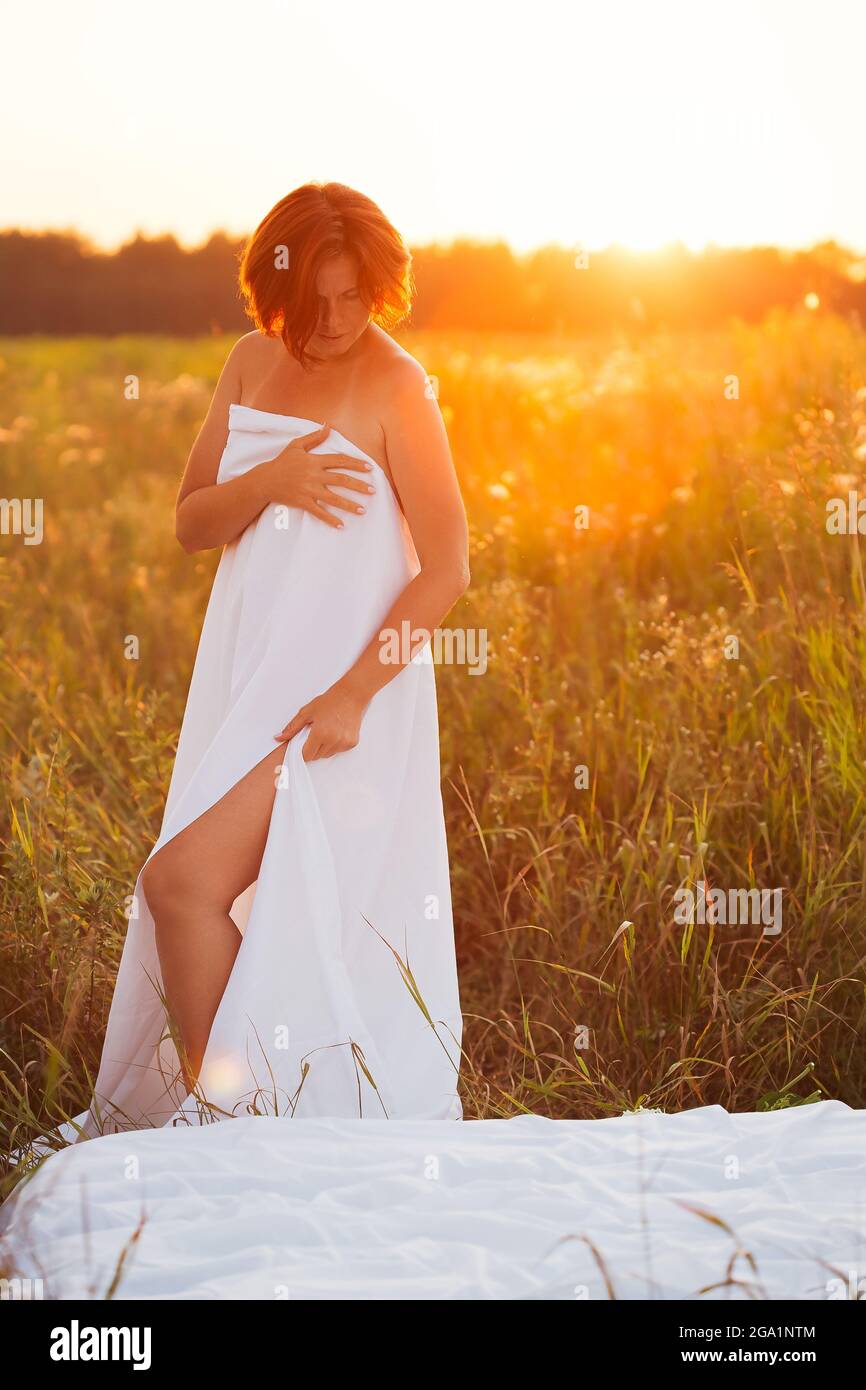 Charming caucasian woman 30-35 years old in a field at sunset in summer ...