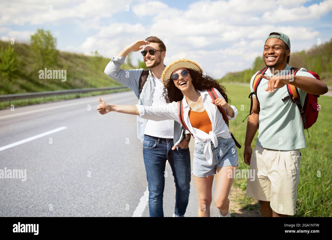 Diverse friends standing on roadside, stopping cars, hitchhiking for ...