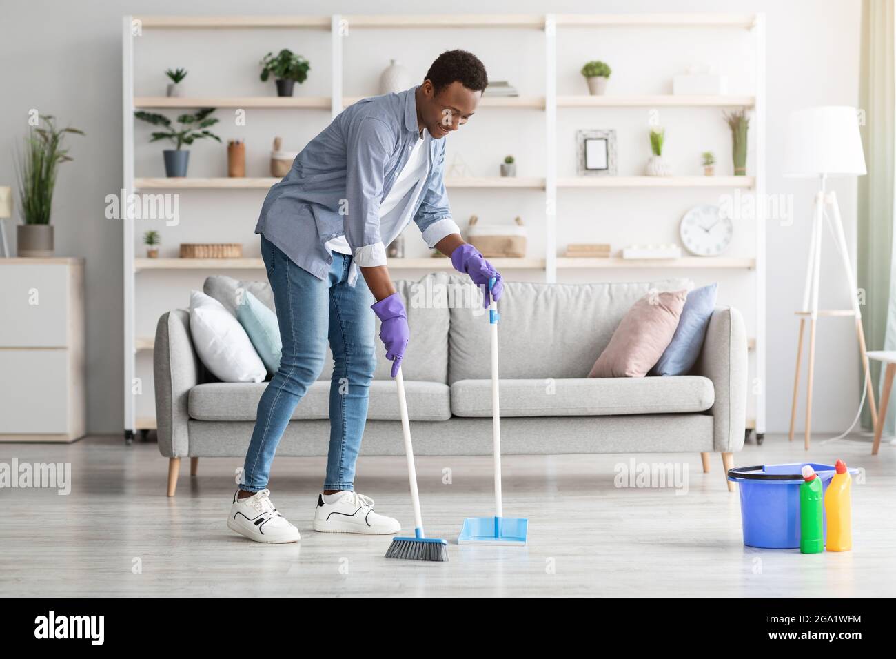 Cheerful black guy cleaning living room, holding broom Stock Photo - Alamy
