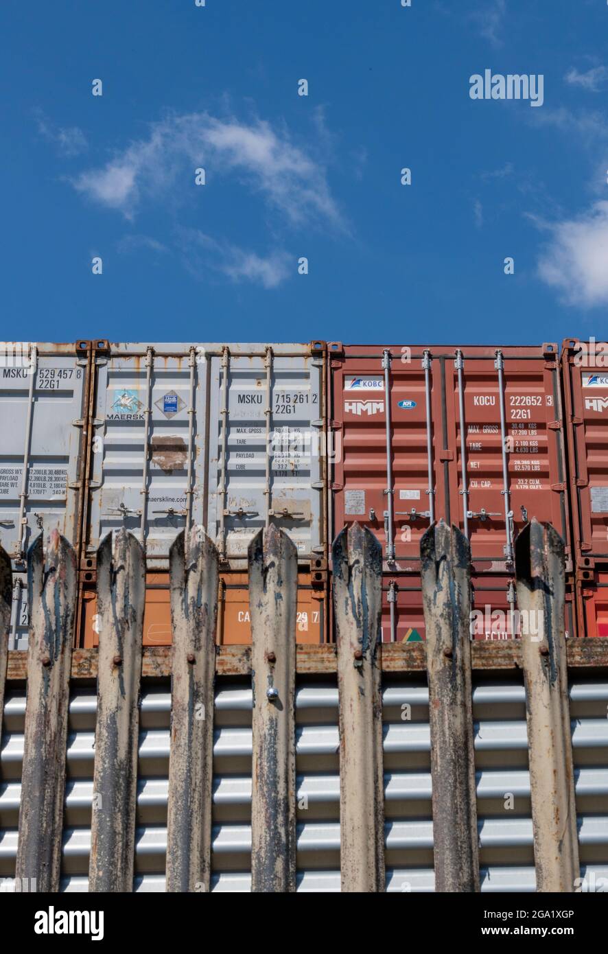 shipping containers stacked in a compound protected by a tall metal ...