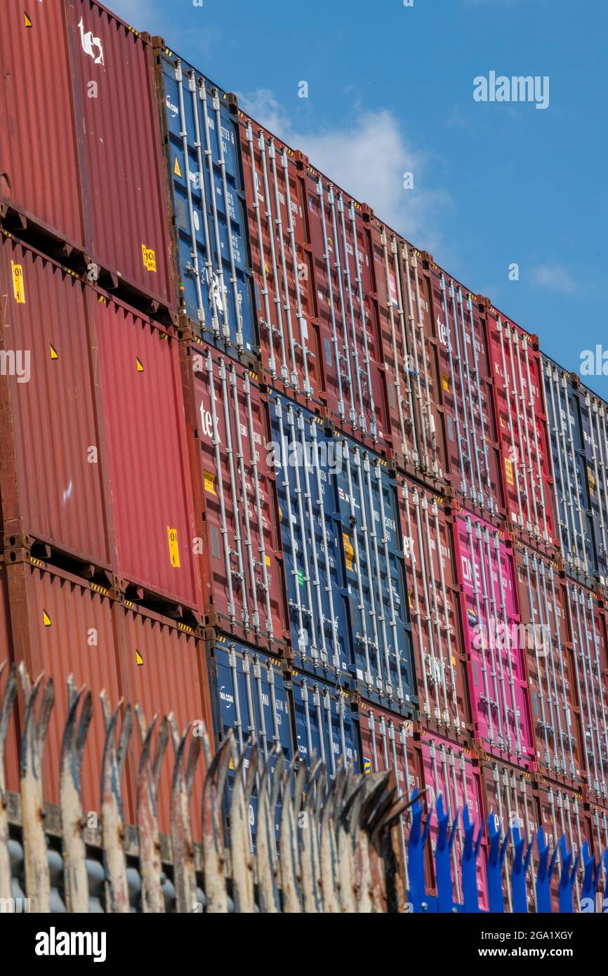 shipping containers stacked in a compound protected by a tall metal ...