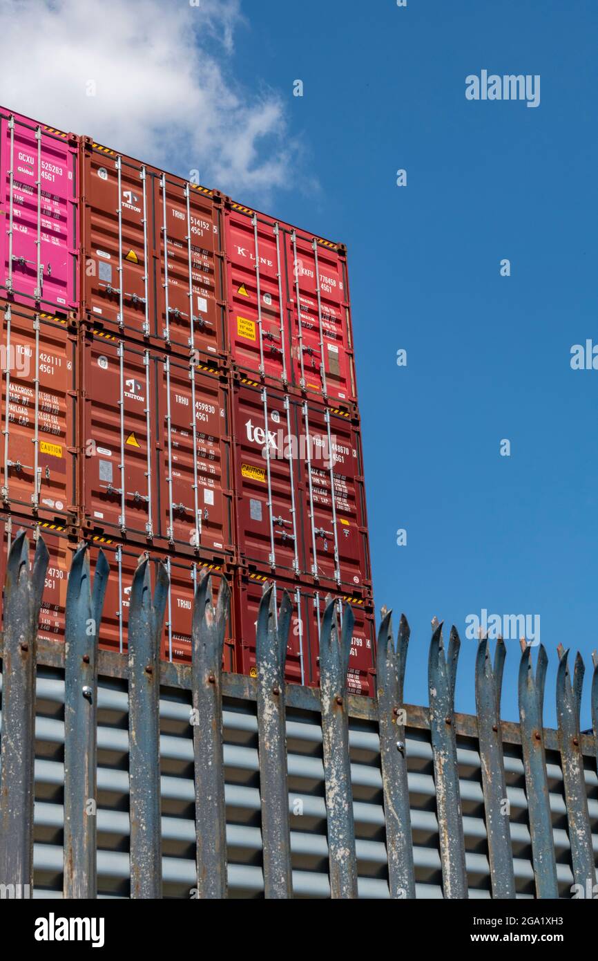 shipping containers stacked in a compound protected by a tall metal ...