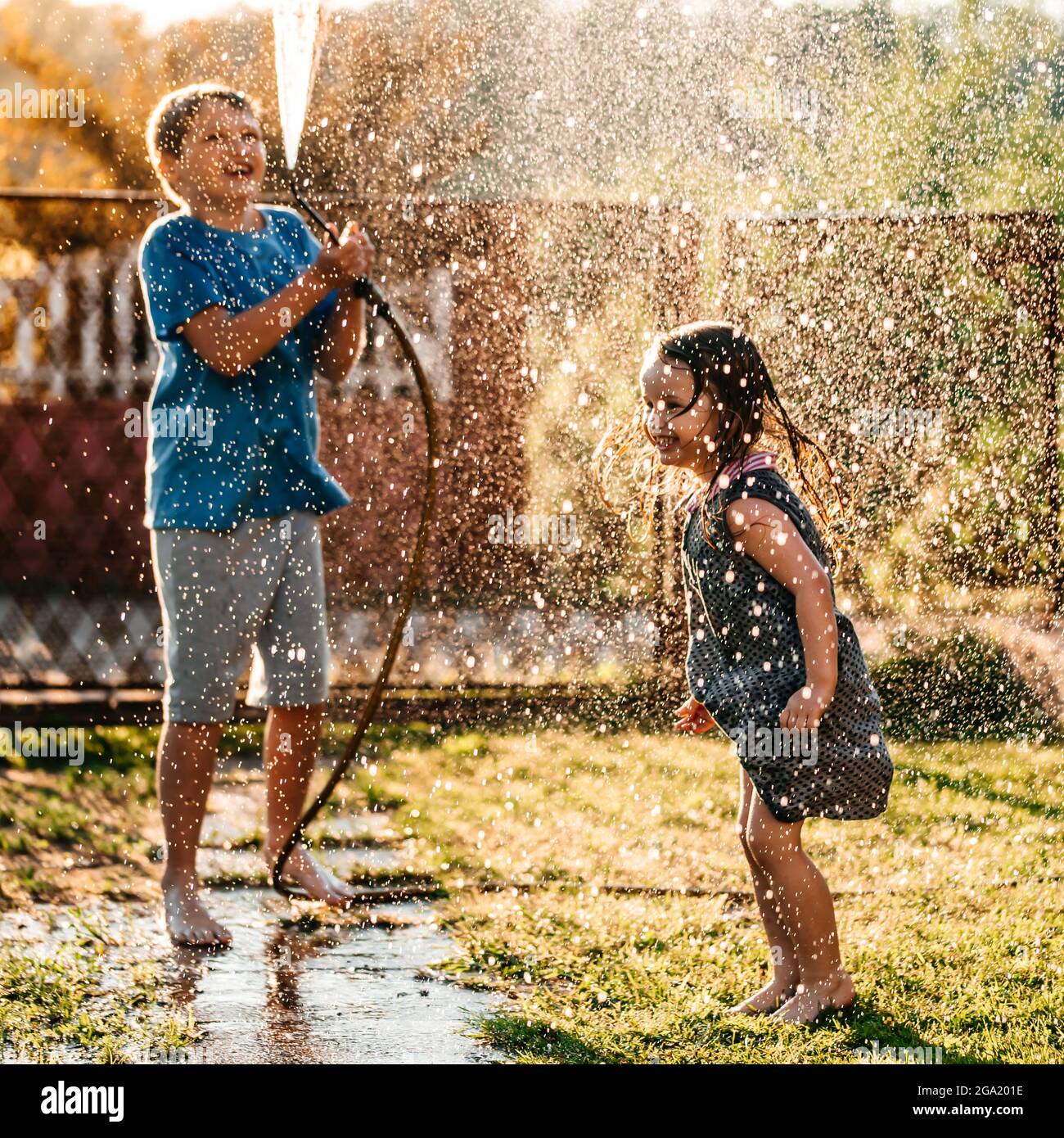little children playing together with a garden hose on hot and sunny ...