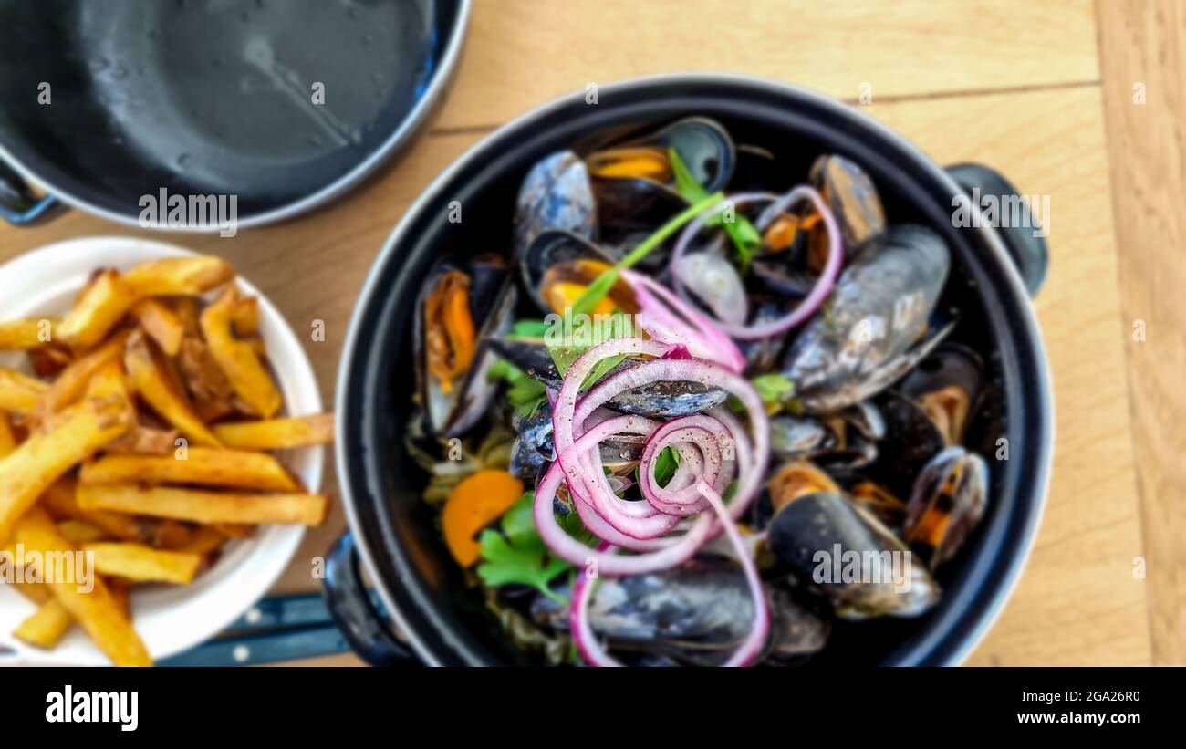 A pot of freshly cooked mussels, fresh purple onion slice and roasted ...