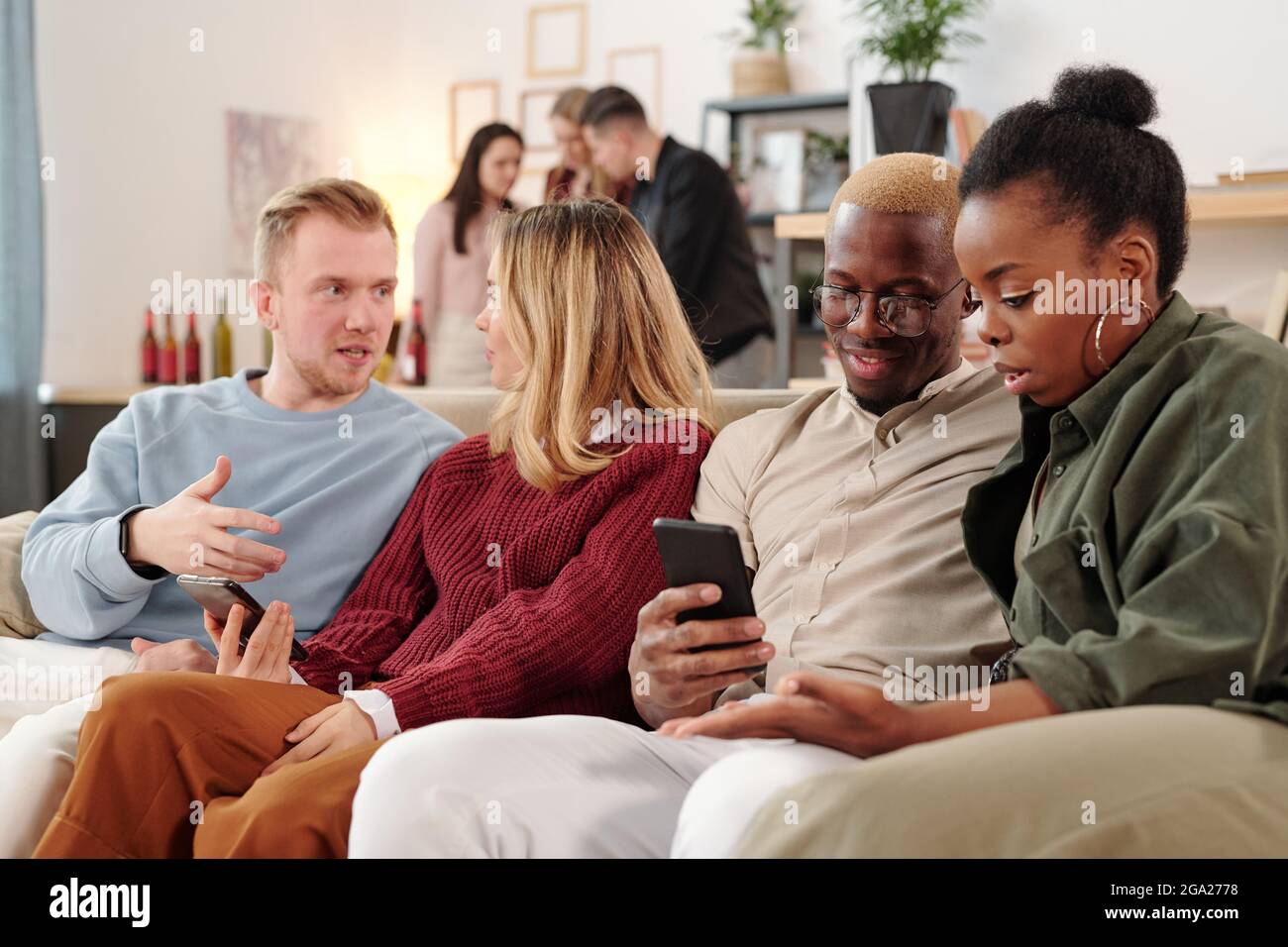 Two young intercultural couples in smart casualwear sitting in row on ...