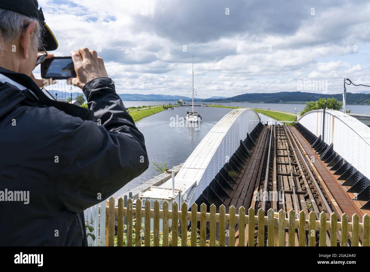 A man photographs the sea lock, a sailboat and railroad bridge of the ...