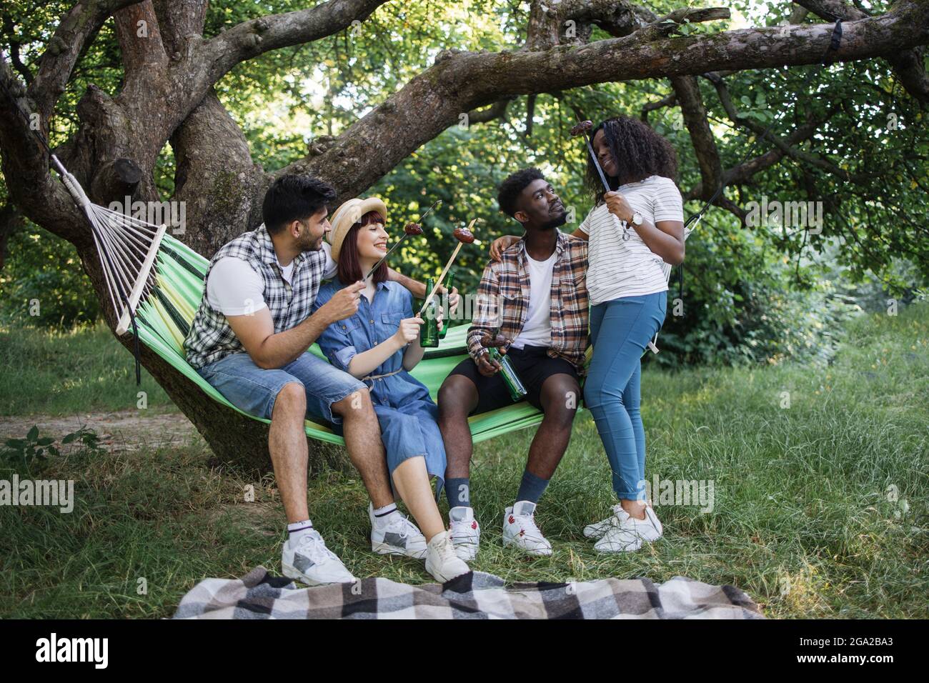 Two multiracial couples having summer picnic outdoors with cold beer ...