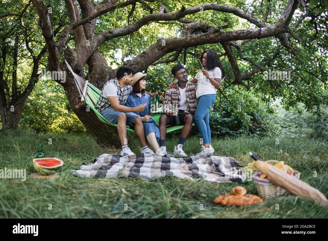 Group of four multicultural friends eating food and drinking beer ...