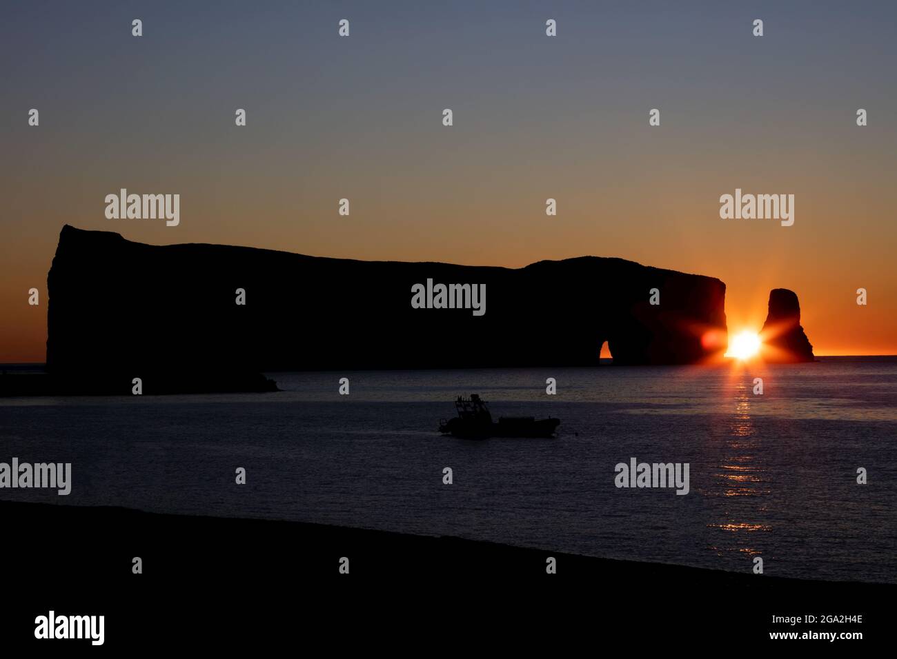 Perce Rock at sunset with the bright sun sinking down over the horizon ...