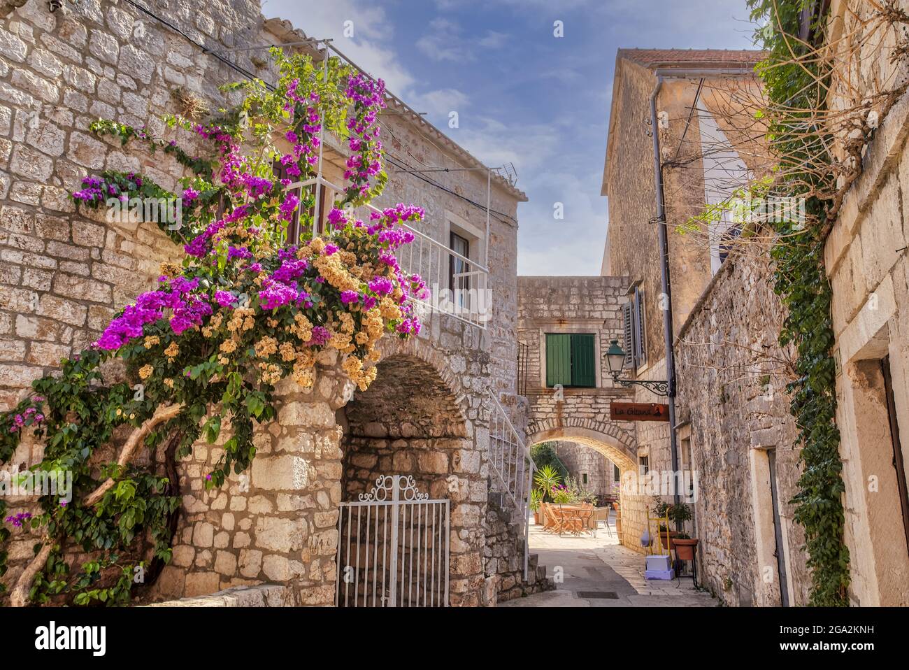 Flowering vines climb up the ancient stone walls along a narrow lane ...
