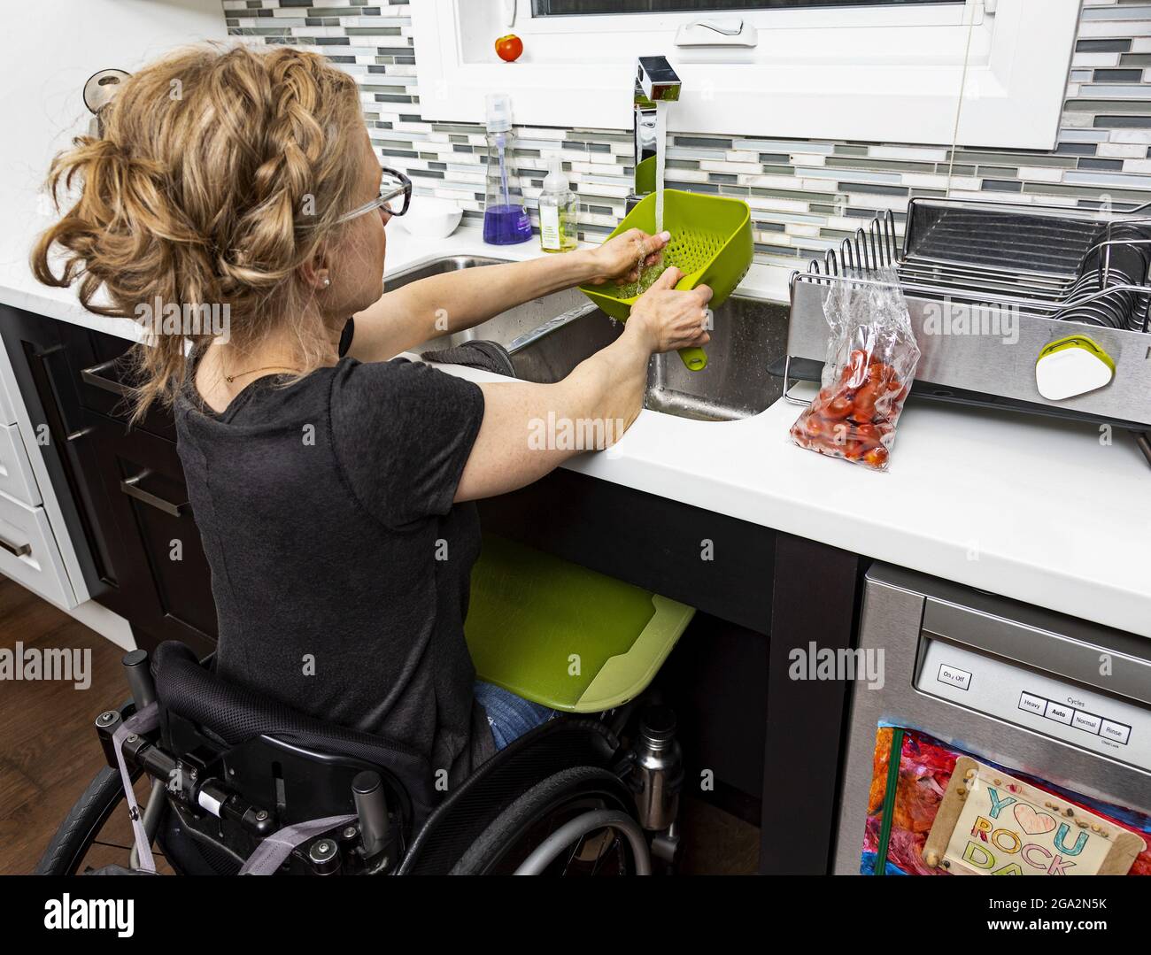 A paraplegic woman rinsing vegetables at the sink while preparing a ...