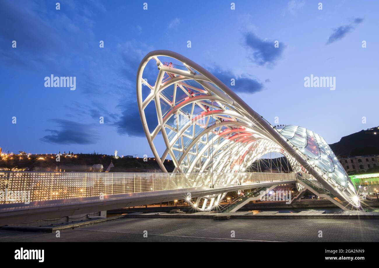 The bow-shaped Bridge of Peace pedestrian bridge, illuminated at dusk ...