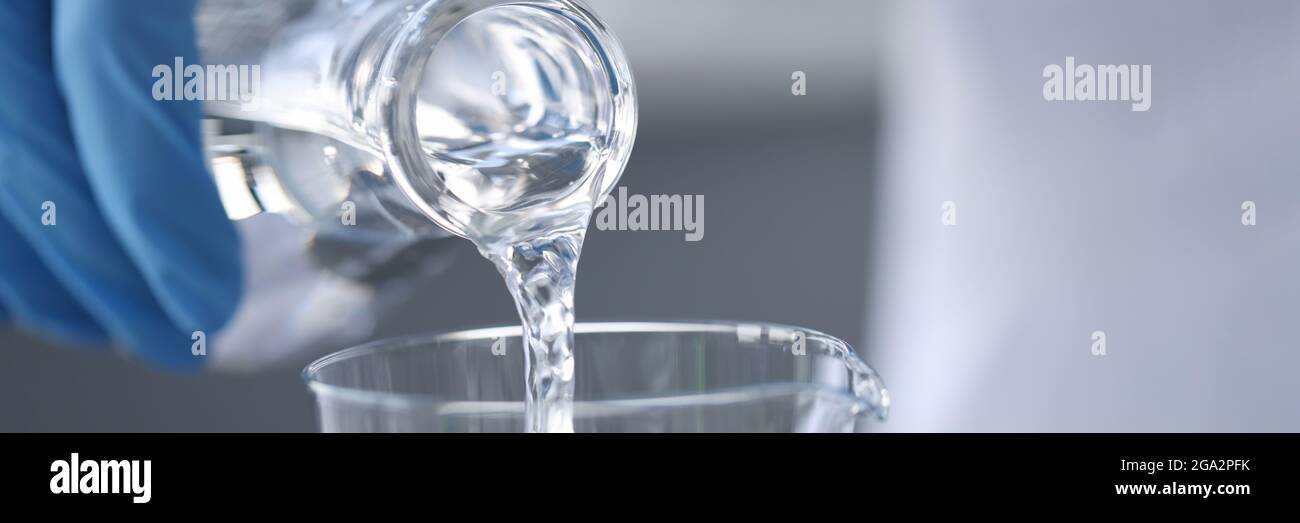 Scientist chemist in gloves pouring water from flask into glass closeup ...