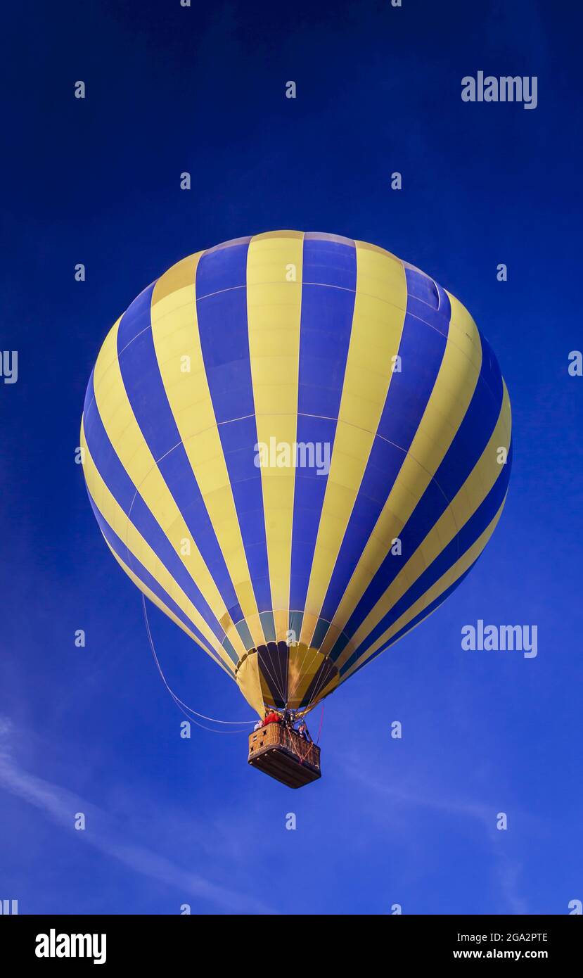 Yellow and blue striped hot air balloon in mid-flight against a blue ...
