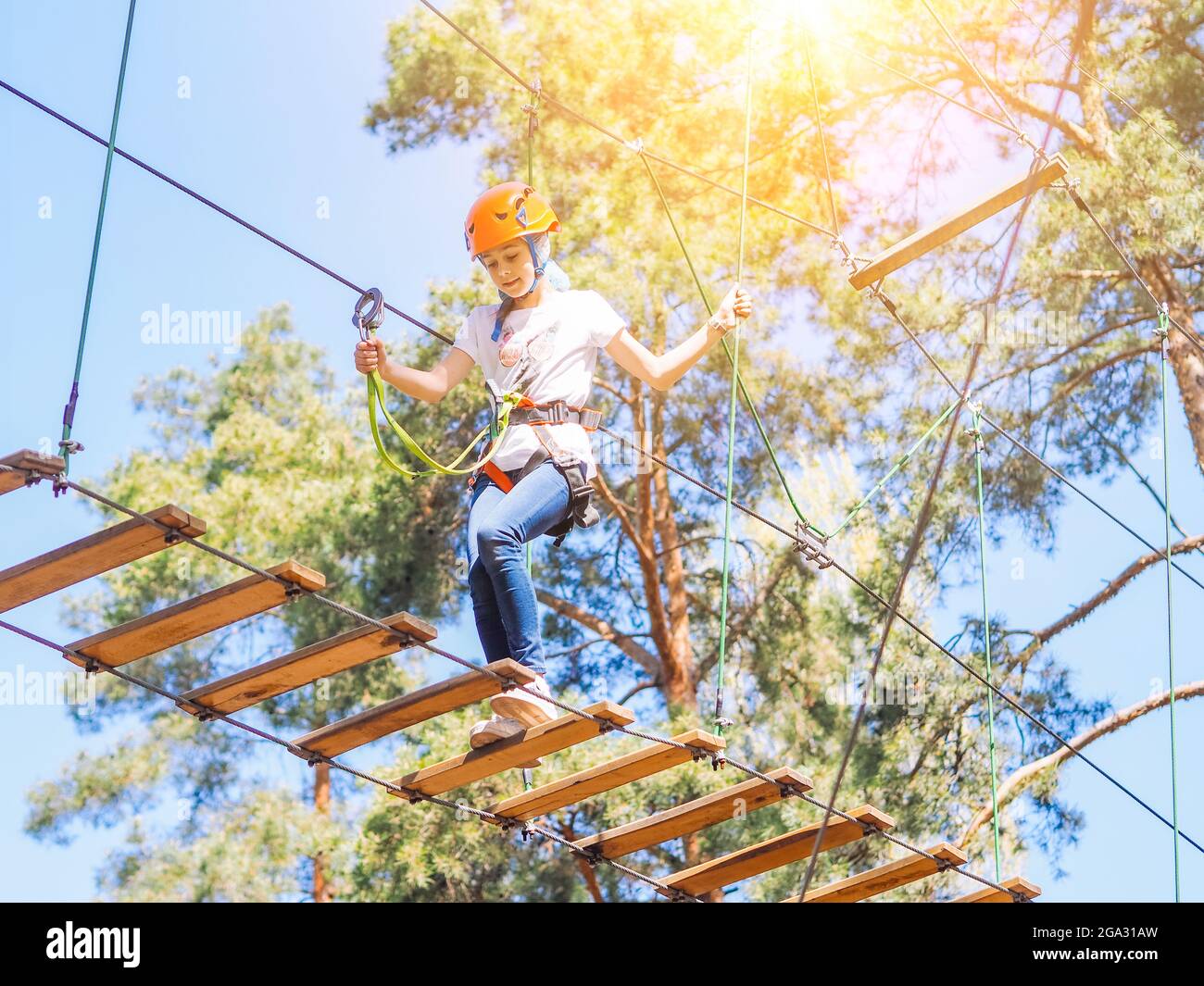 Kid in orange helmet climbing in trees on forest adventure park. Girl ...