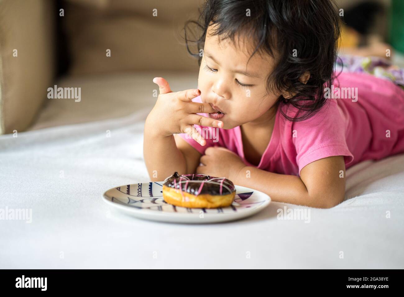 Sweet Southeast Asian female child eating a donut Stock Photo - Alamy