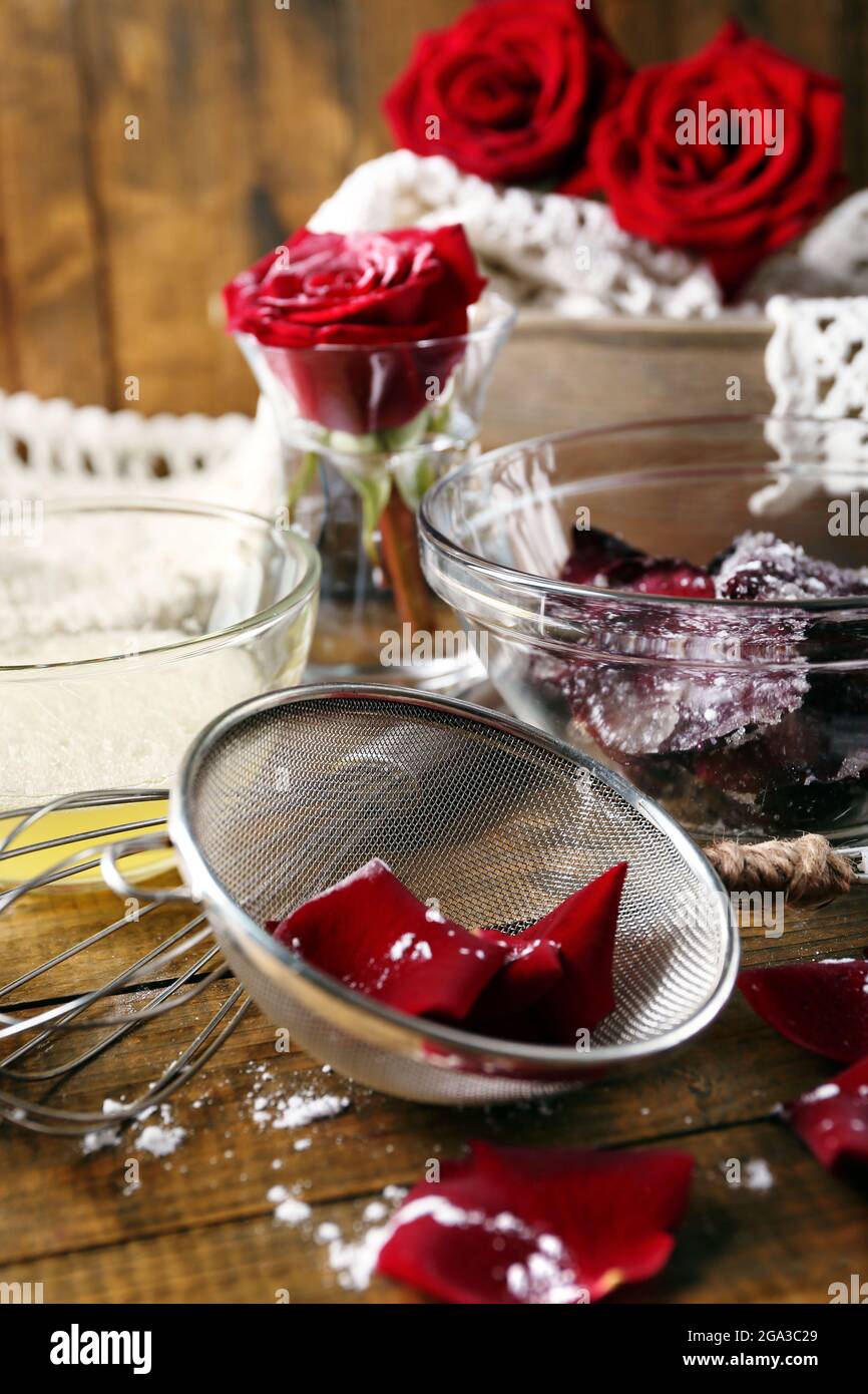 Making candied rose flower petals with egg whites and sugar, on wooden ...