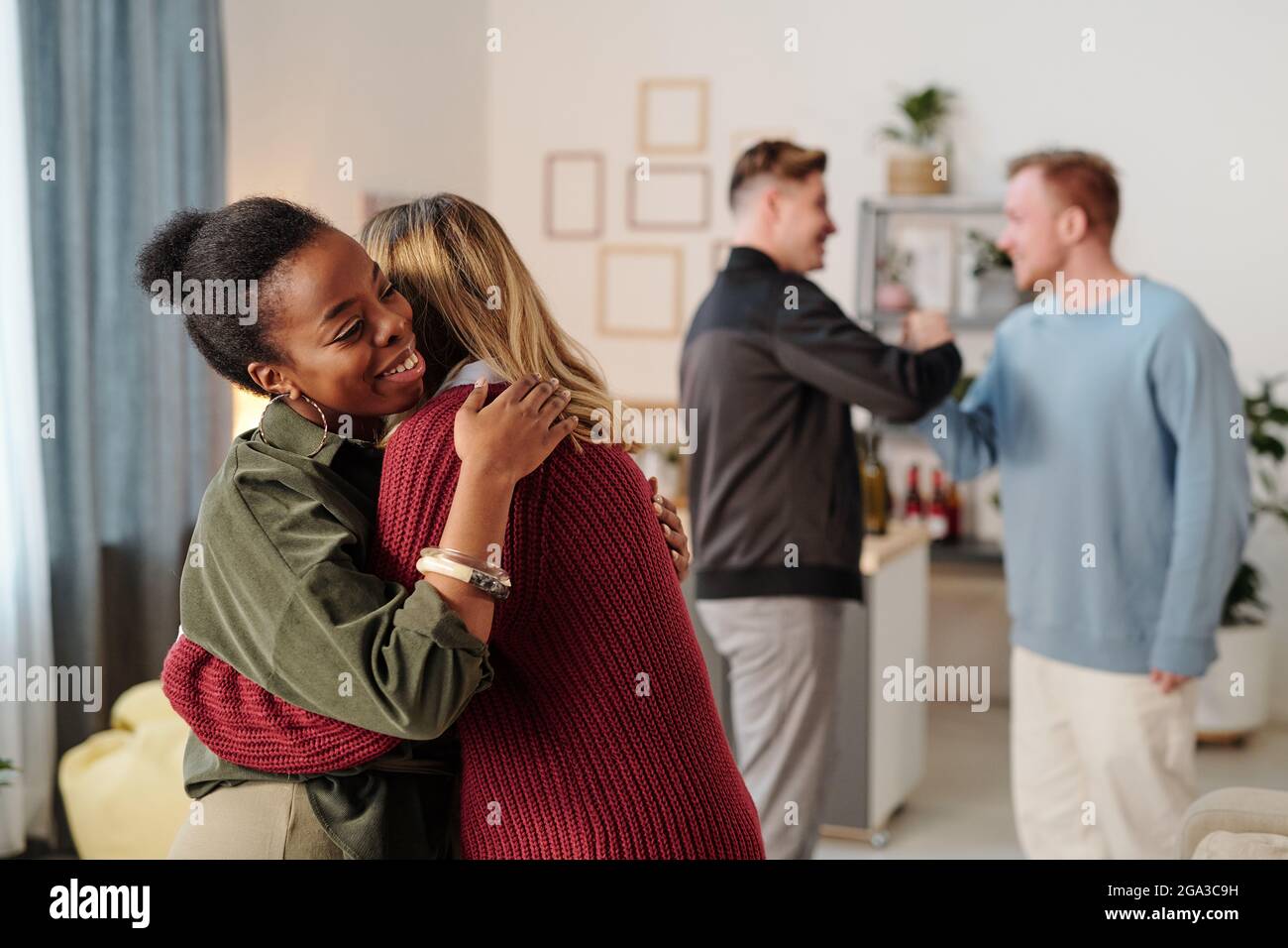 Happy young African woman in smart casualwear giving hug to guy in blue ...