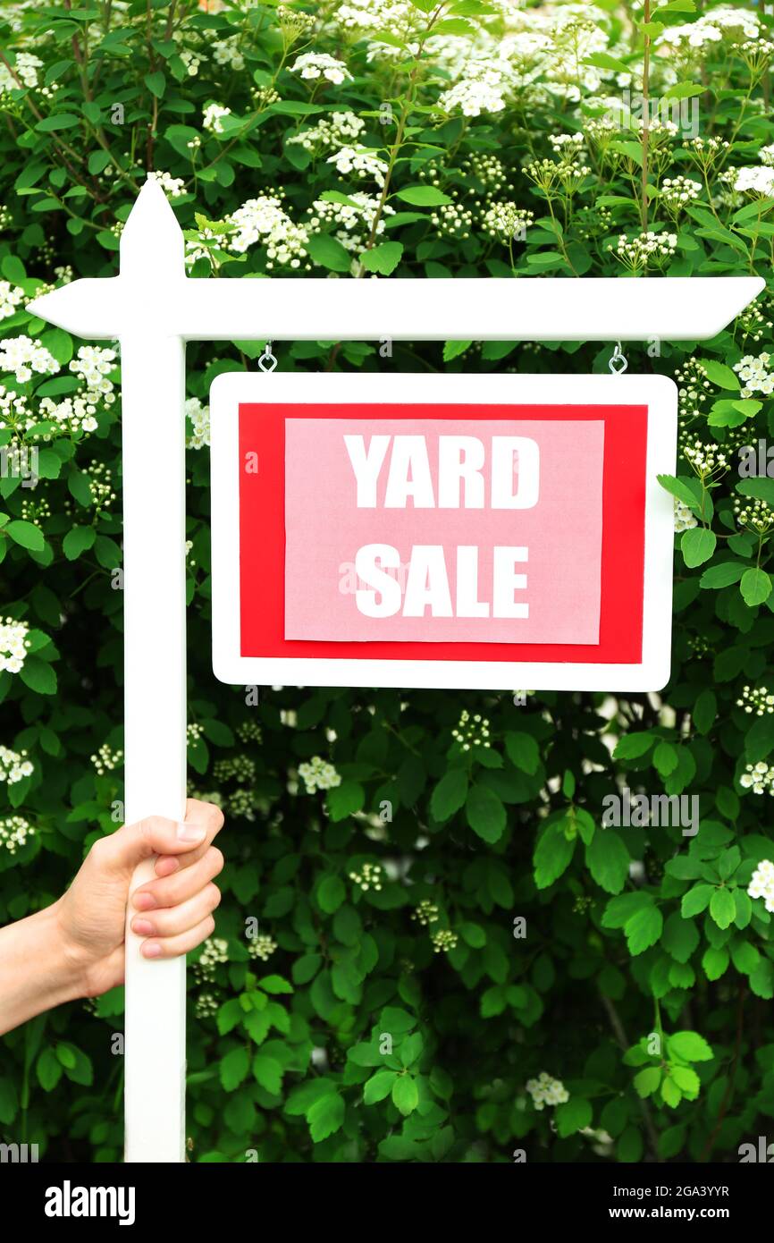 Wooden Yard Sale sign in female hand over green bush and flowers ...