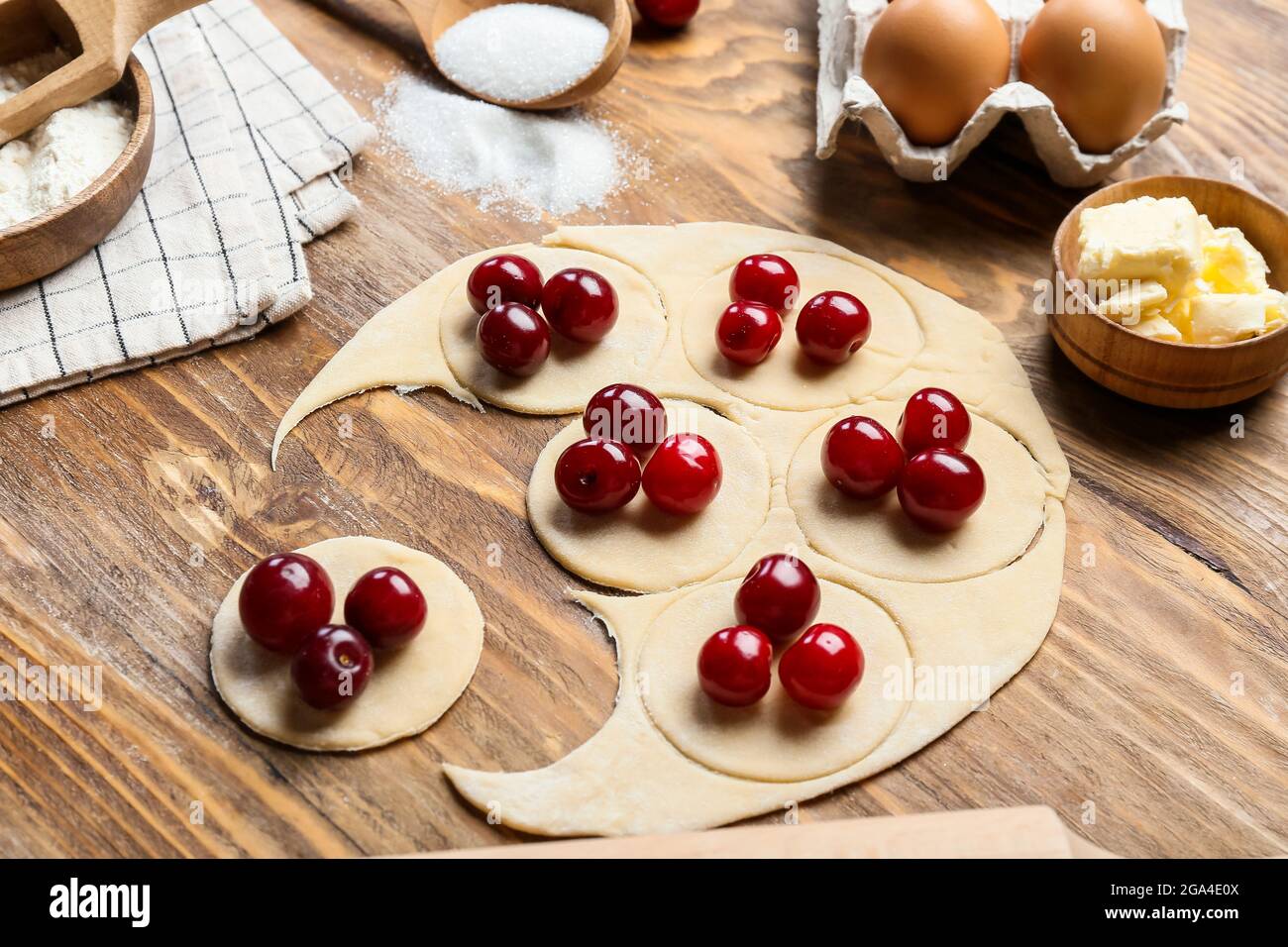 Fresh dough for cherry dumplings and ingredients on wooden background ...