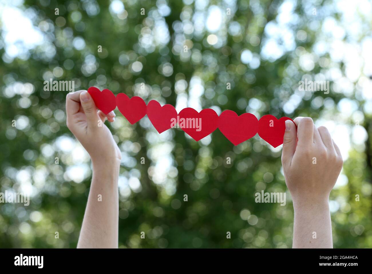 Female hands with chain of paper hearts over nature background Stock ...