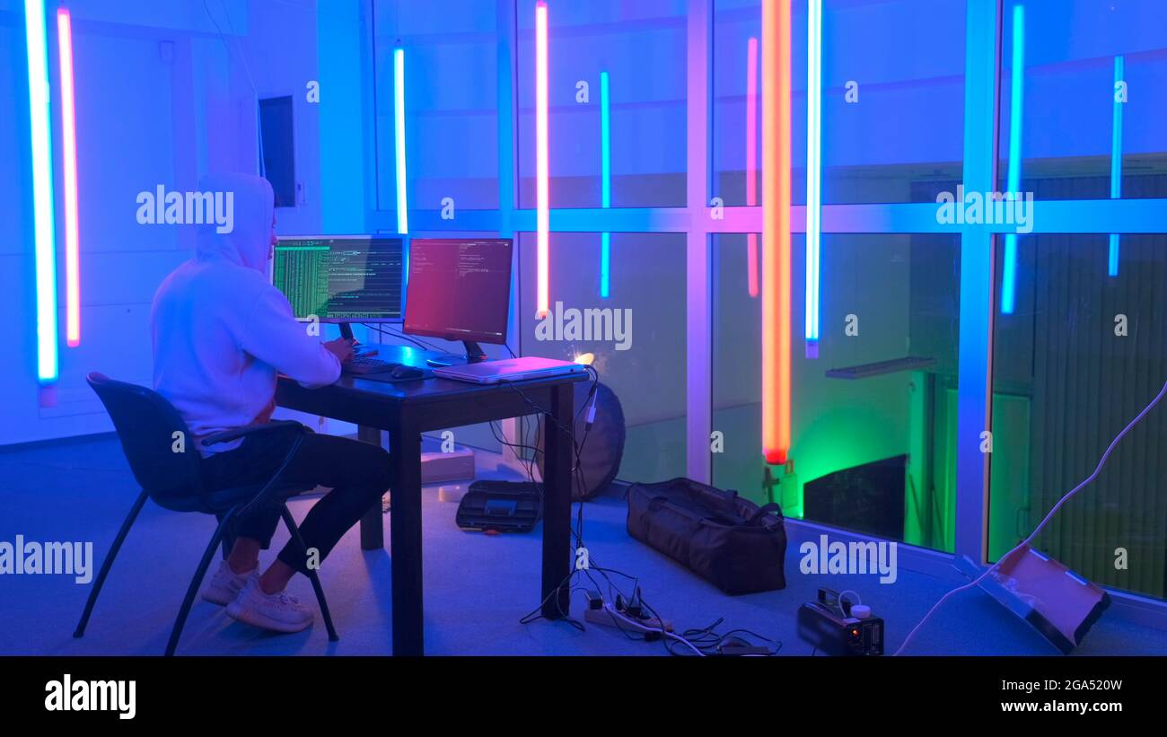 Hacker working place: hacker working in a room with colored neon lights ...