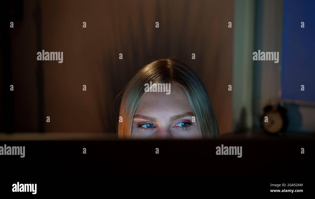 Crop view of beautiful female sitting at night at computer and looking ...