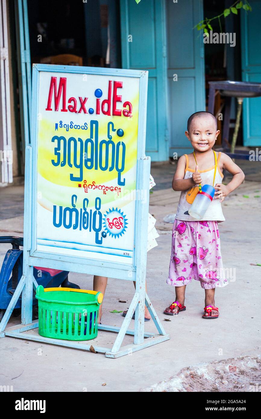Young Burmese girl with shaved head wearing pyjamas stands next to ...