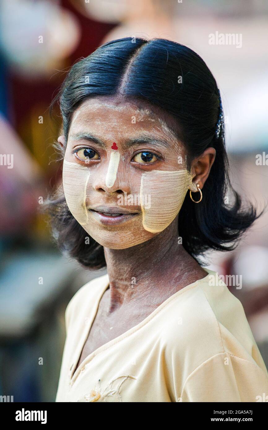 Beautiful young Burmese girl with thanaka yellow paste on cheeks and yellow eyes poses for photo ...