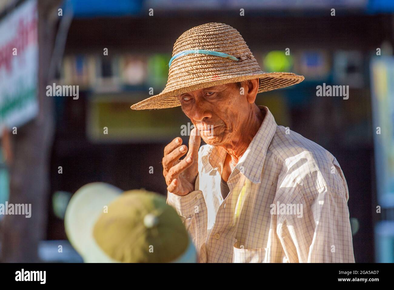 Elderly Burmese man with eye cataract wears straw hat, manual labour ...