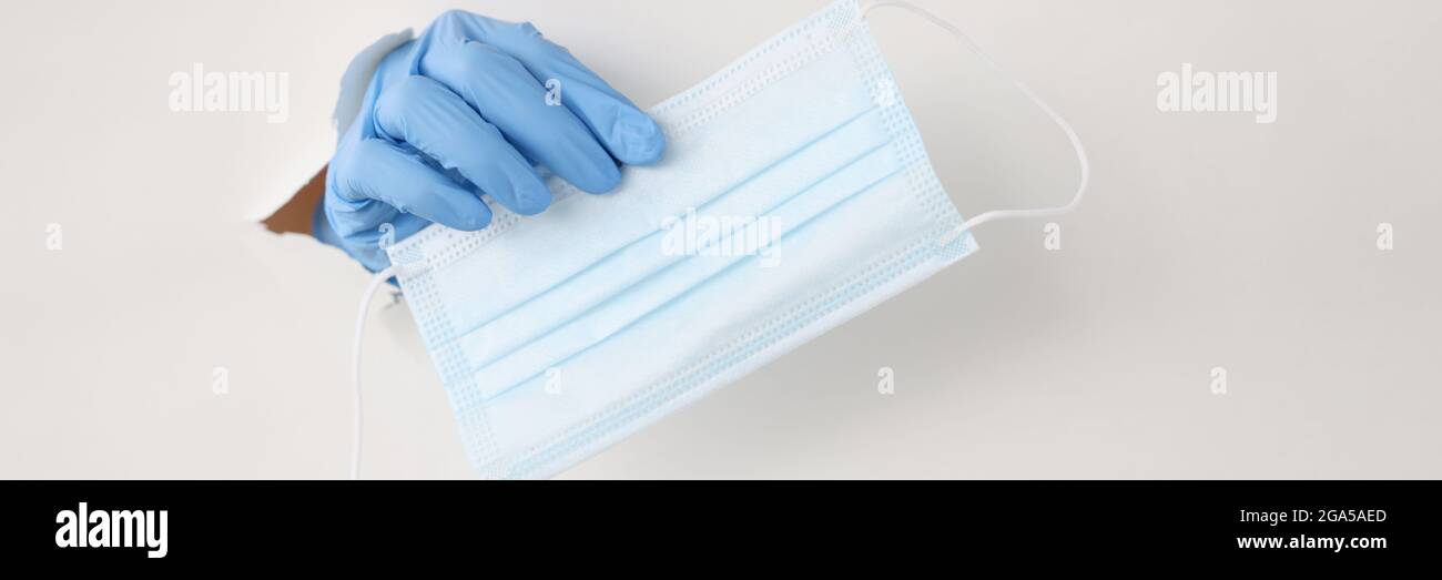 Hand in rubber glove pull out medical protective mask from torn paper ...