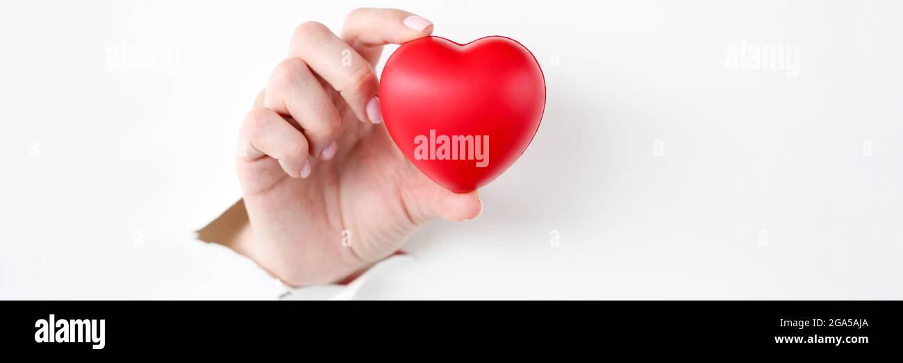 Hand pulling out toy red heart from torn paper Stock Photo - Alamy