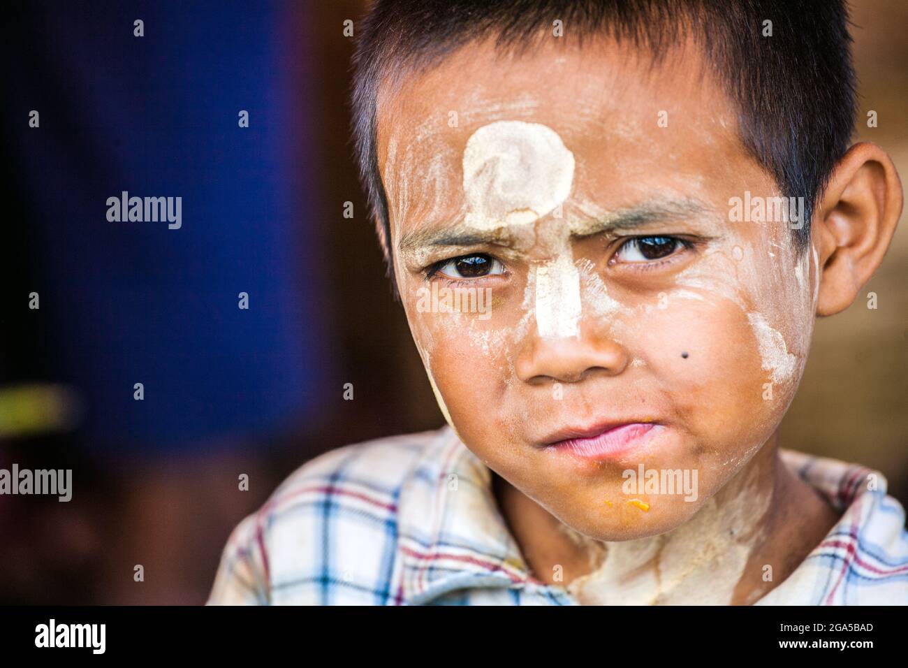 Cute young Burmese boy with thanaka face powder stares into camera ...