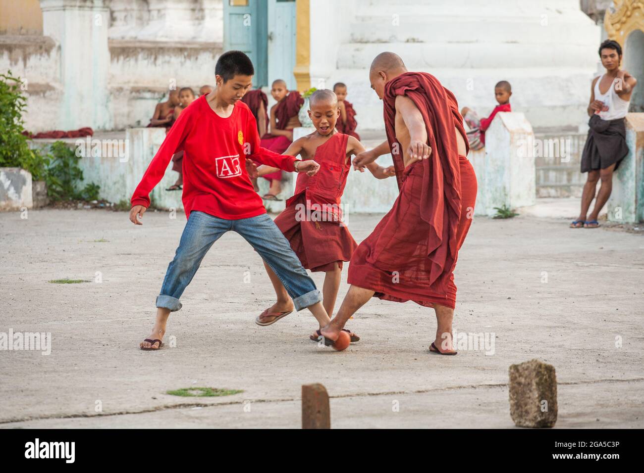 Group of young Burmese monks wearing maroon robes playing football at ...