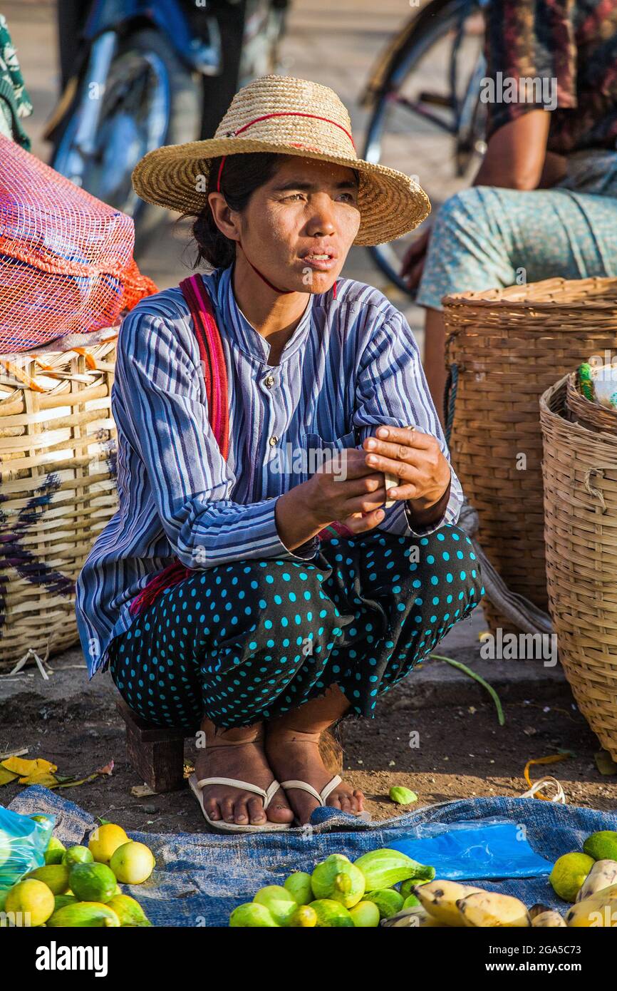 Female market trader wearing straw hat crouched by fruit on ground ...