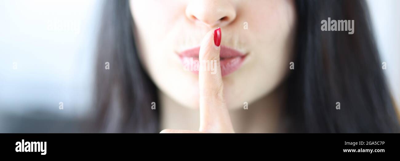 Young woman holding index finger near lips closeup Stock Photo - Alamy