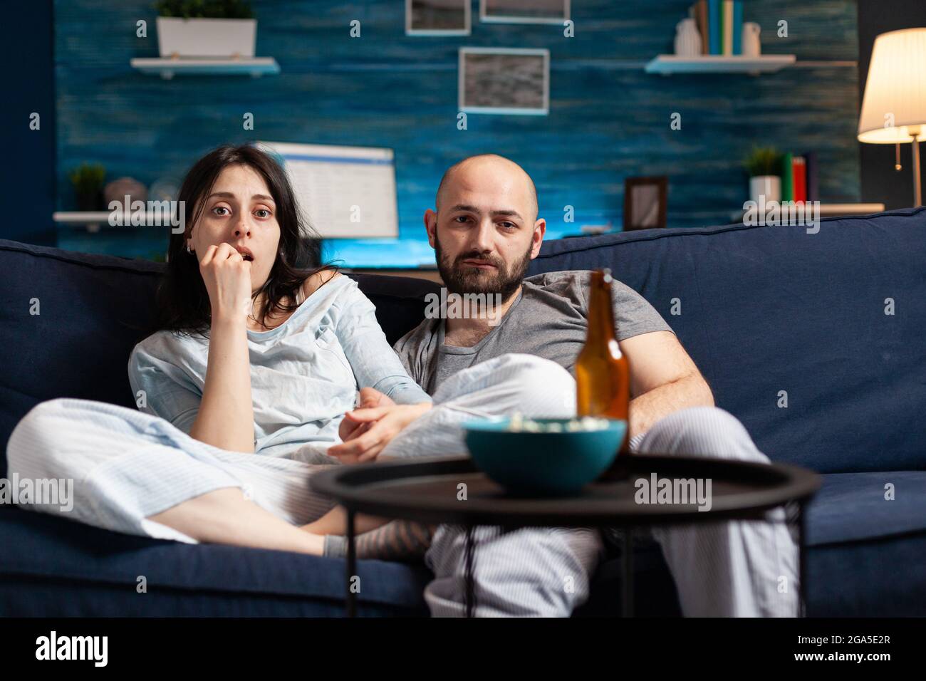 Sensitive sad couple watching drama movie on television sitting on sofa ...