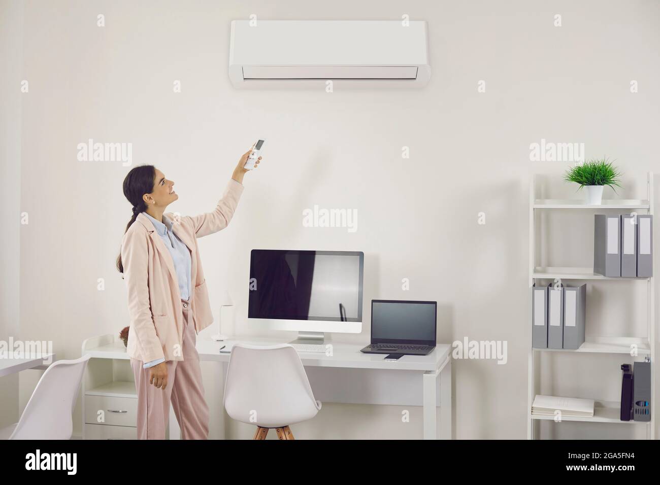 Woman using remote control to switch wall air conditioner in modern ...