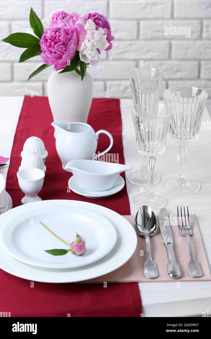 Beautiful table setting with flowers in vase on brick wall background ...