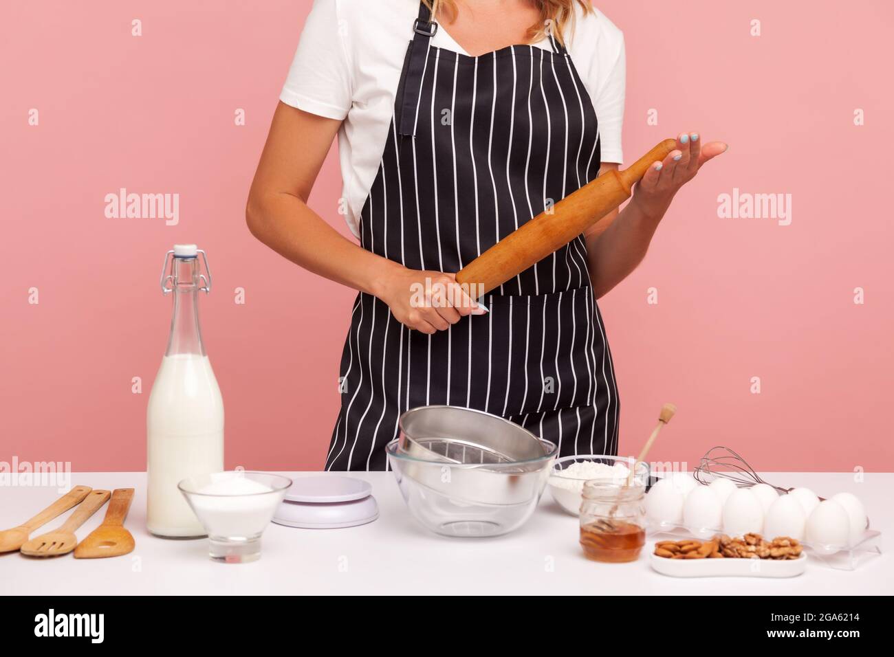 Cropped image of baker in striped apron, holding rolling pin in hands, being surrounded with ...