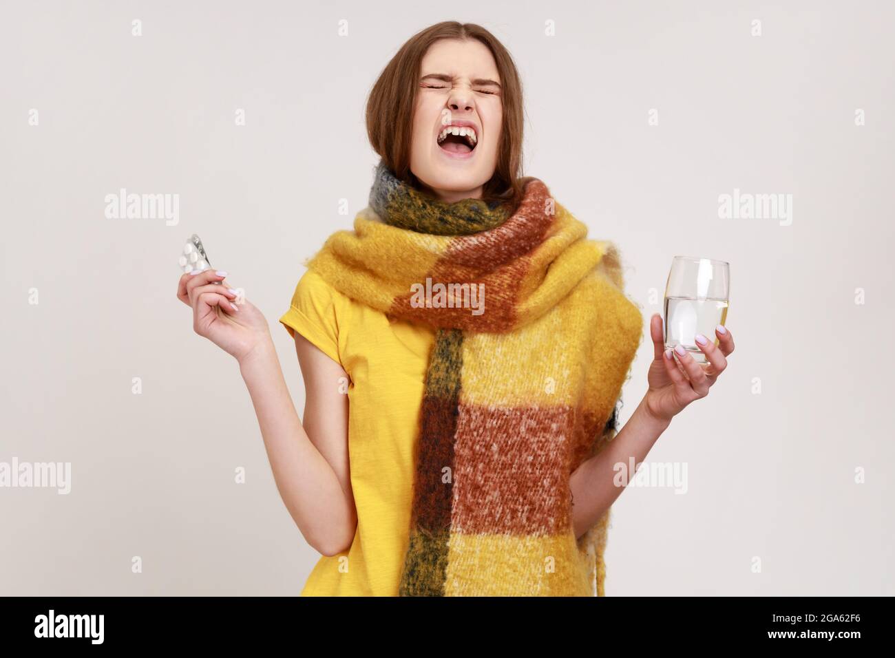Portrait of flu-sick teenager girl wrapped in scarf holding pills and ...