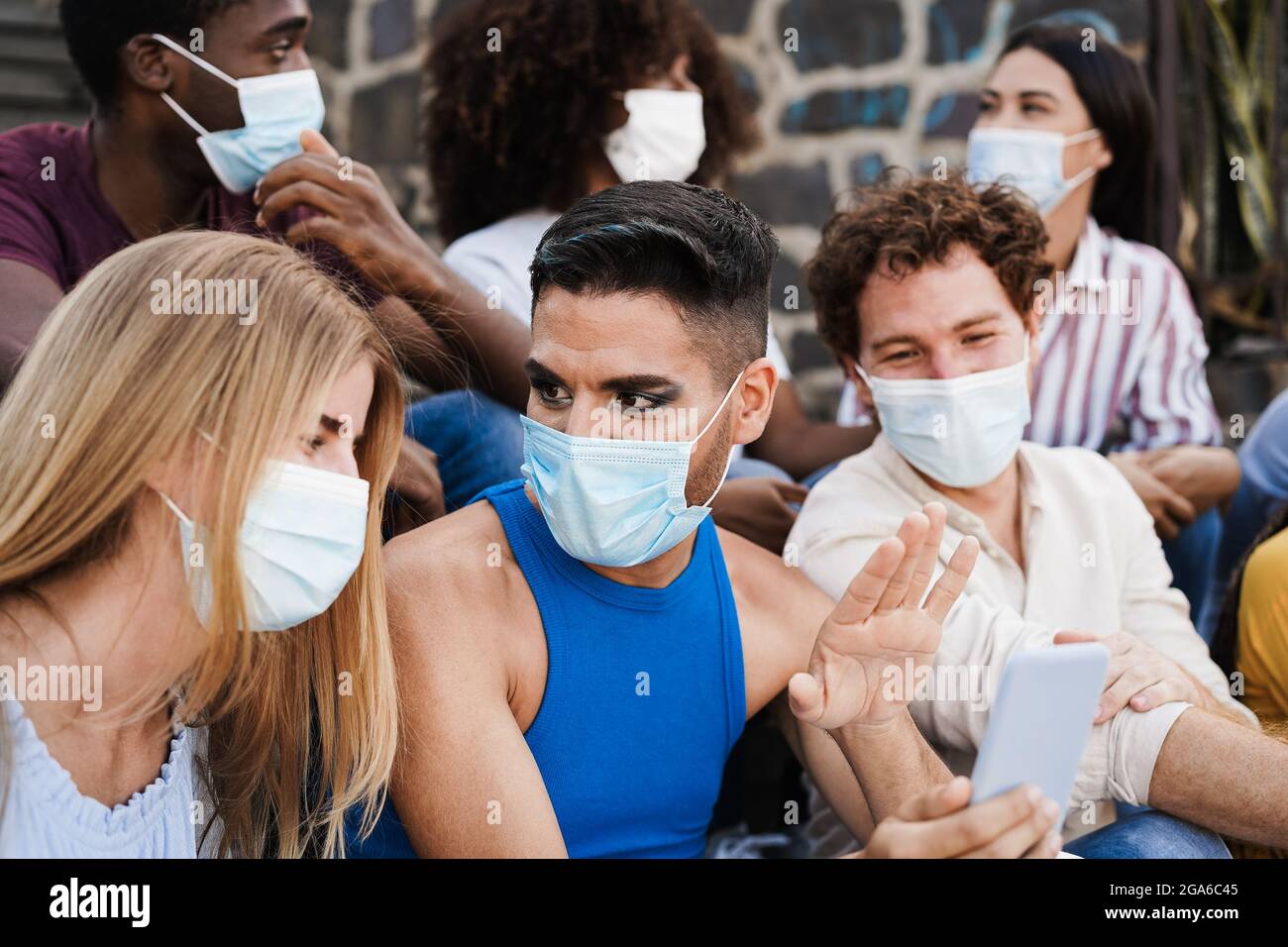 Young diverse people having fun together wearing safety masks outdoor ...
