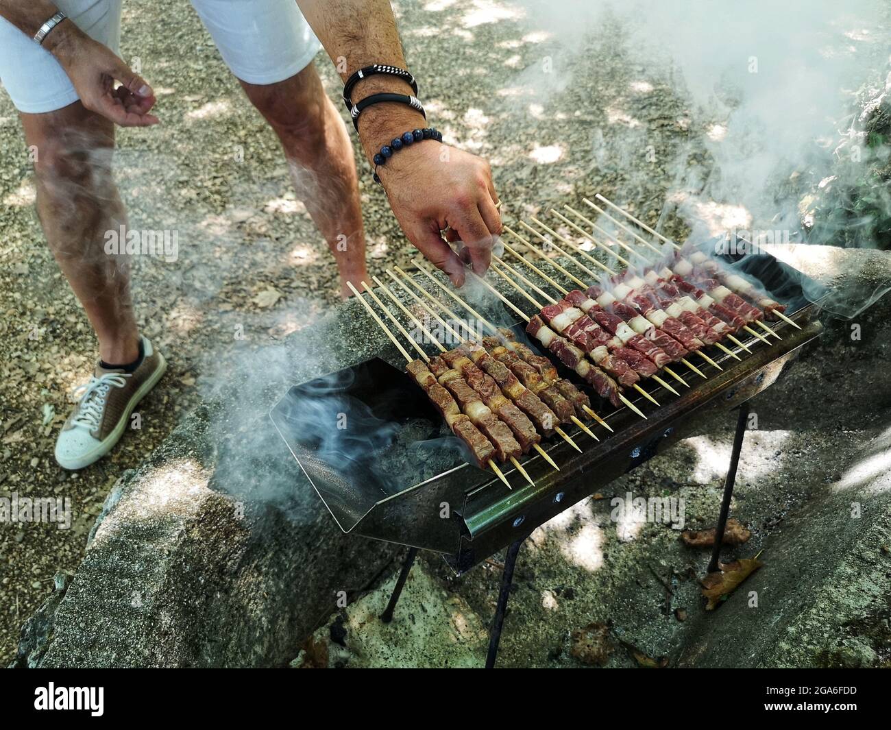 Guy grilling skewers of meat outdoors during a picnic Stock Photo - Alamy