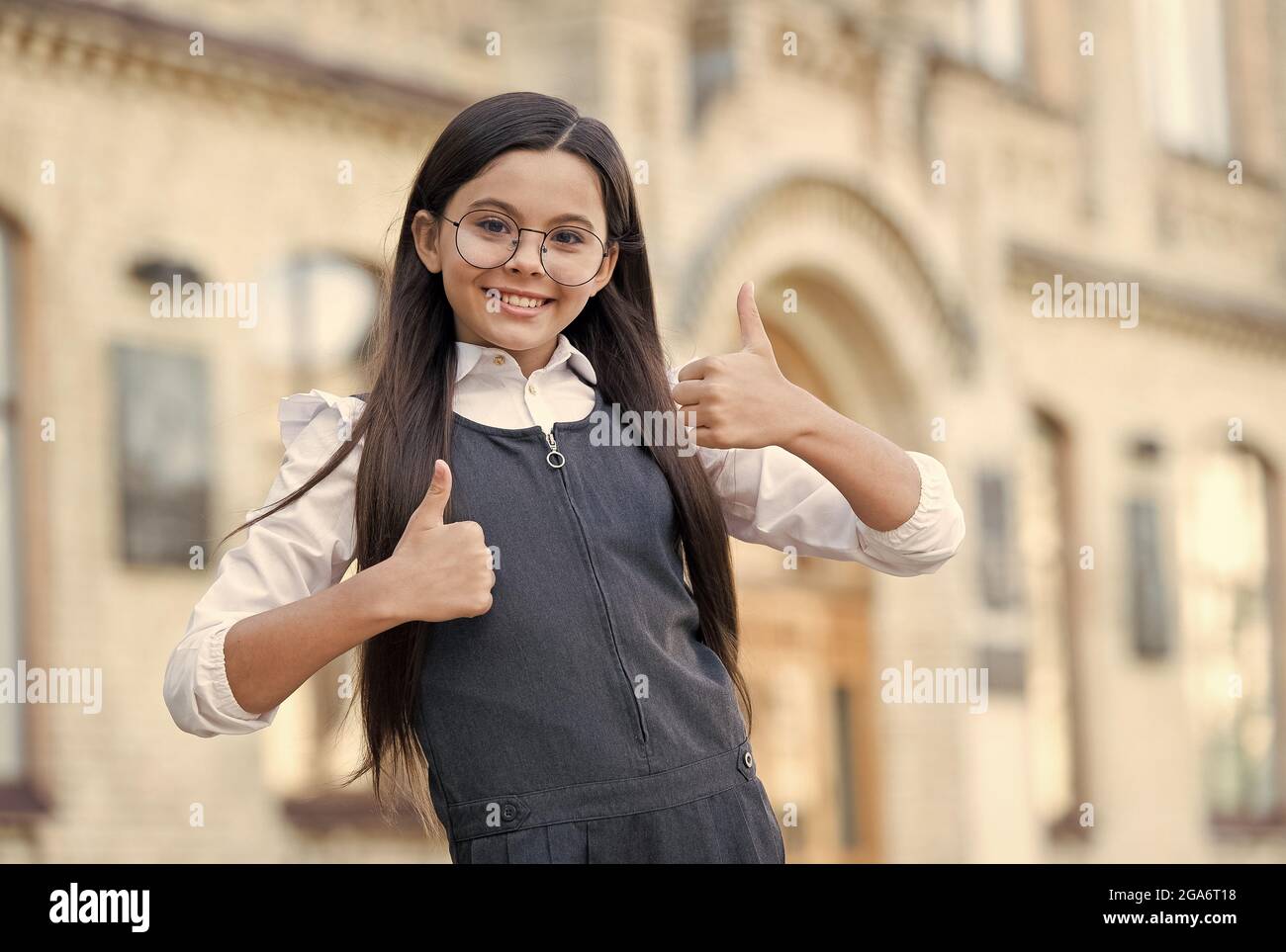 Happy child in school uniform give thumbs ups hand gesture in ...